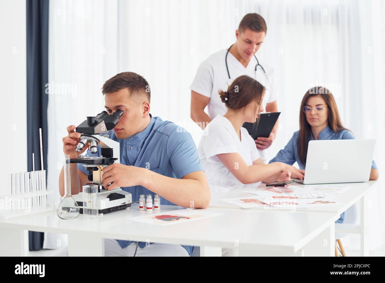 Using microscope. Group of young doctors is working together in the ...