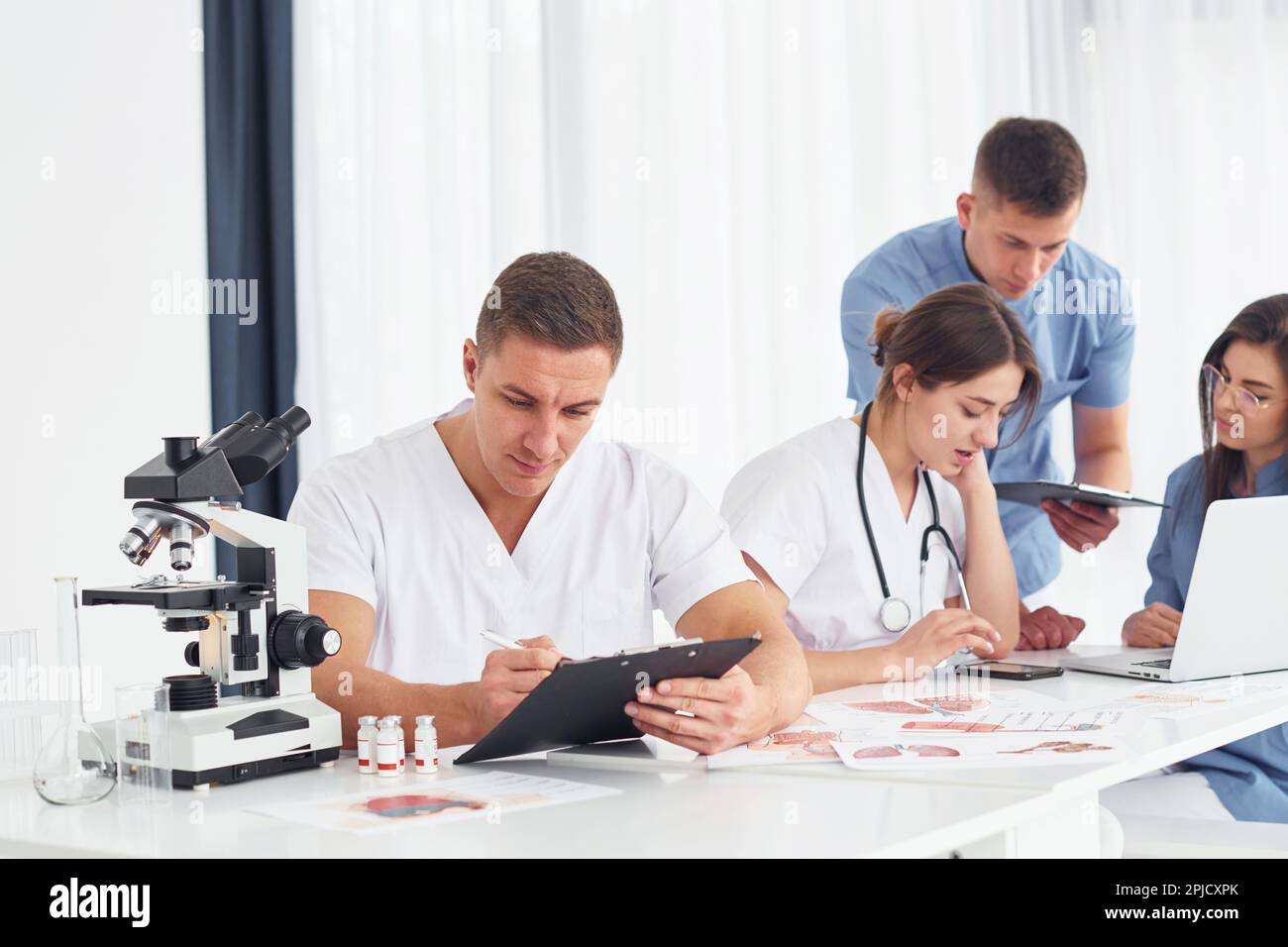 Using microscope. Group of young doctors is working together in the ...