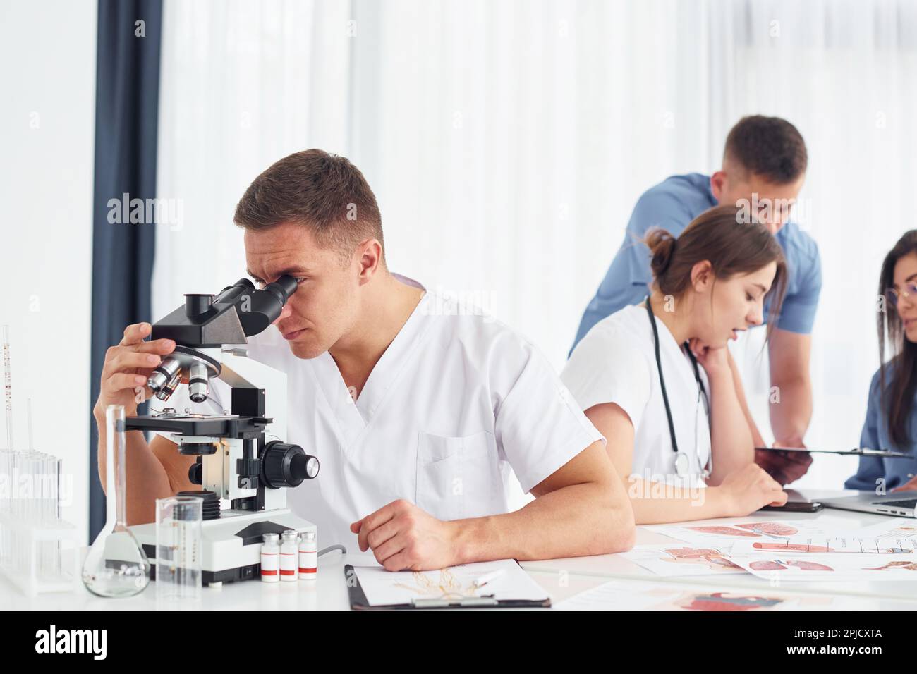 Man with microscope. Group of young doctors is working together in the ...