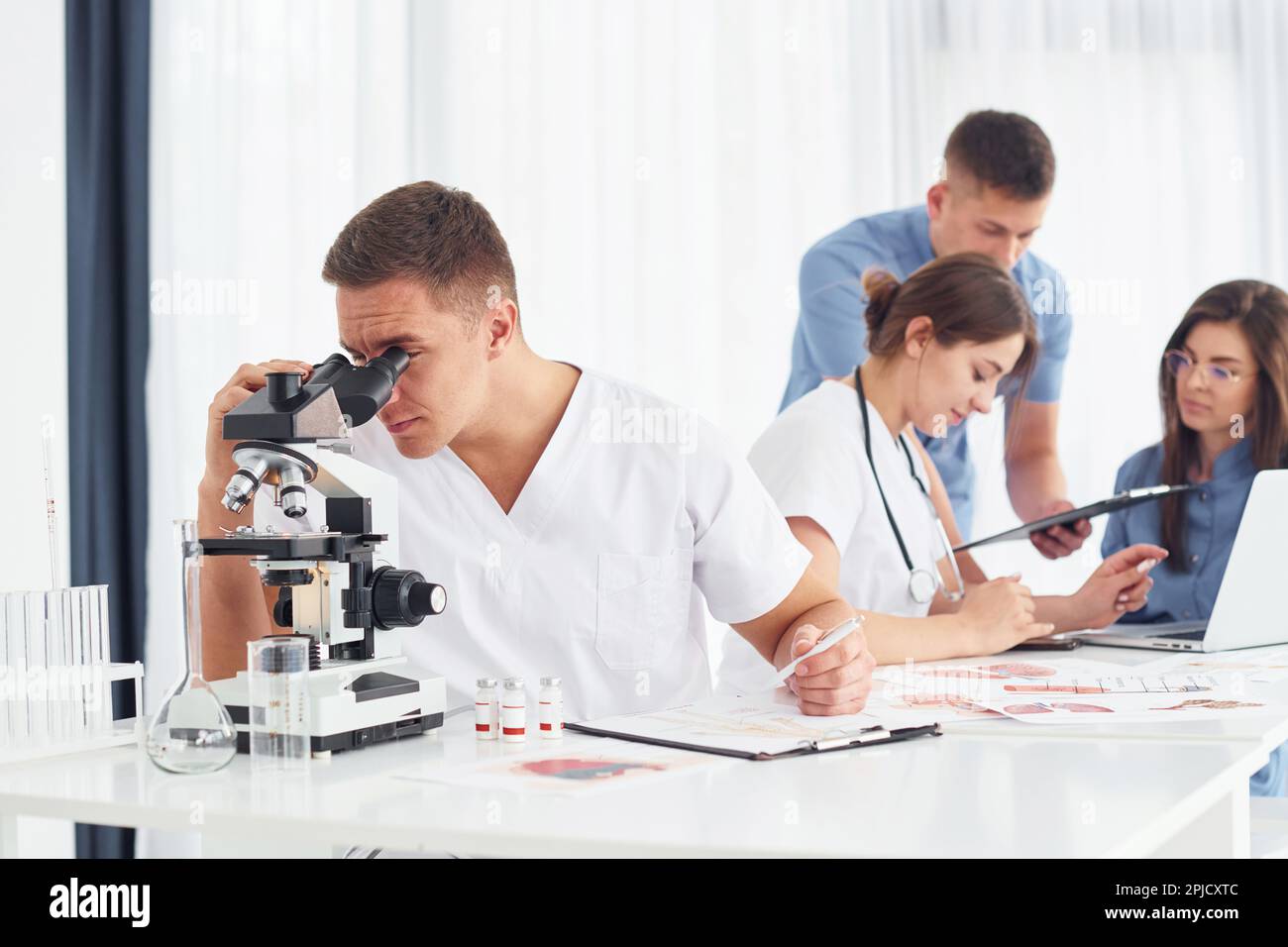 Man with microscope. Group of young doctors is working together in the ...