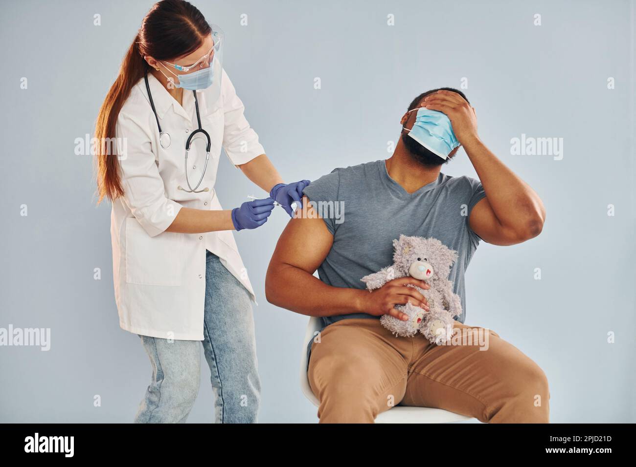 Scared guy with teddy bear. Female doctor giving injection to african ...