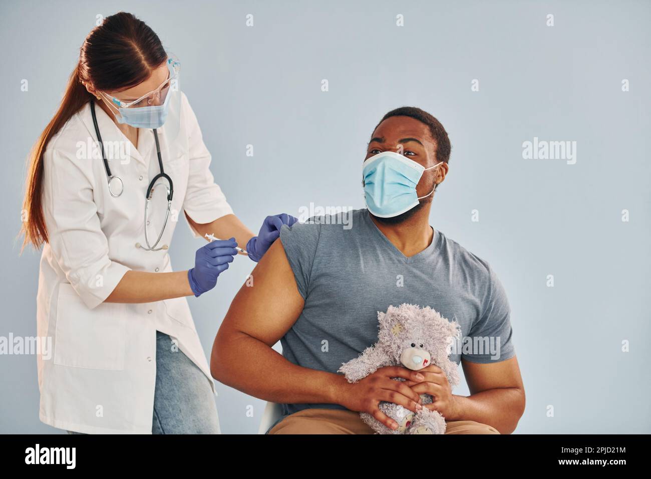 Scared guy with teddy bear. Female doctor giving injection to african ...
