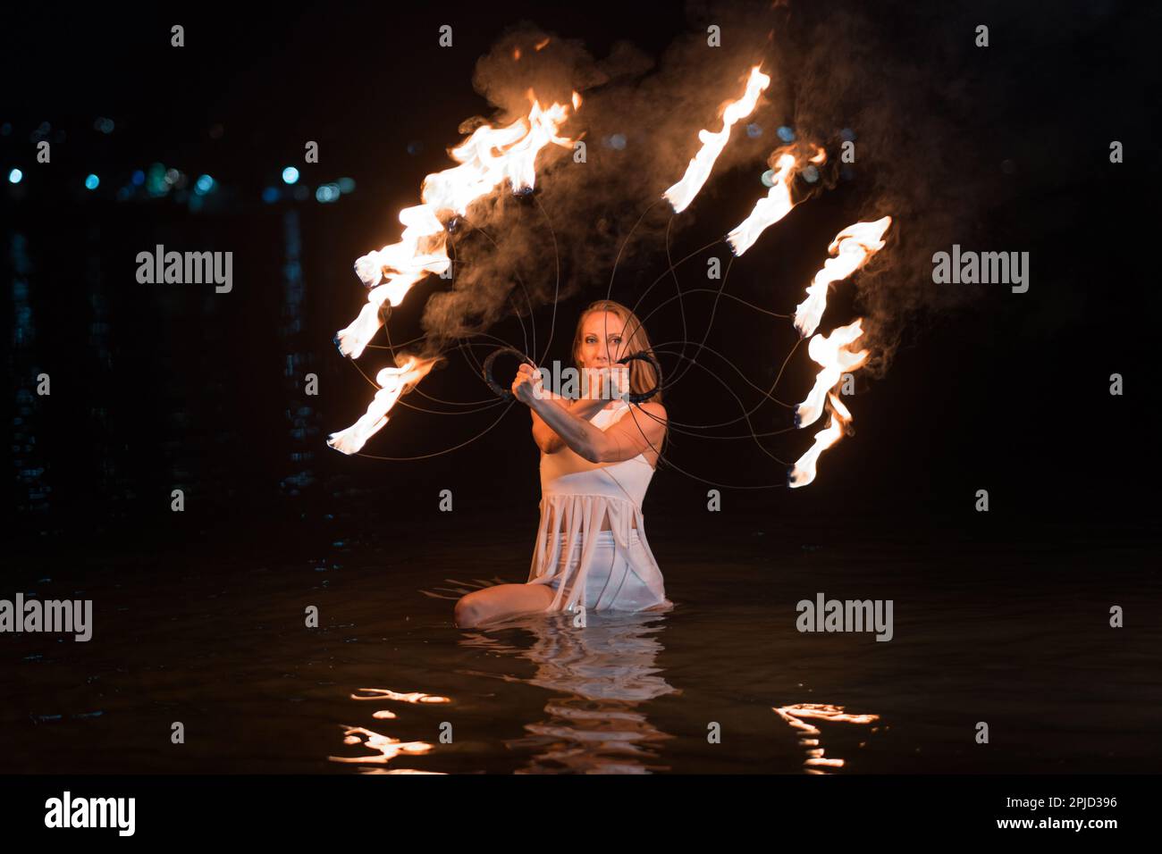 Caucasian woman dancing with fire in the water. Fire show at sea ...