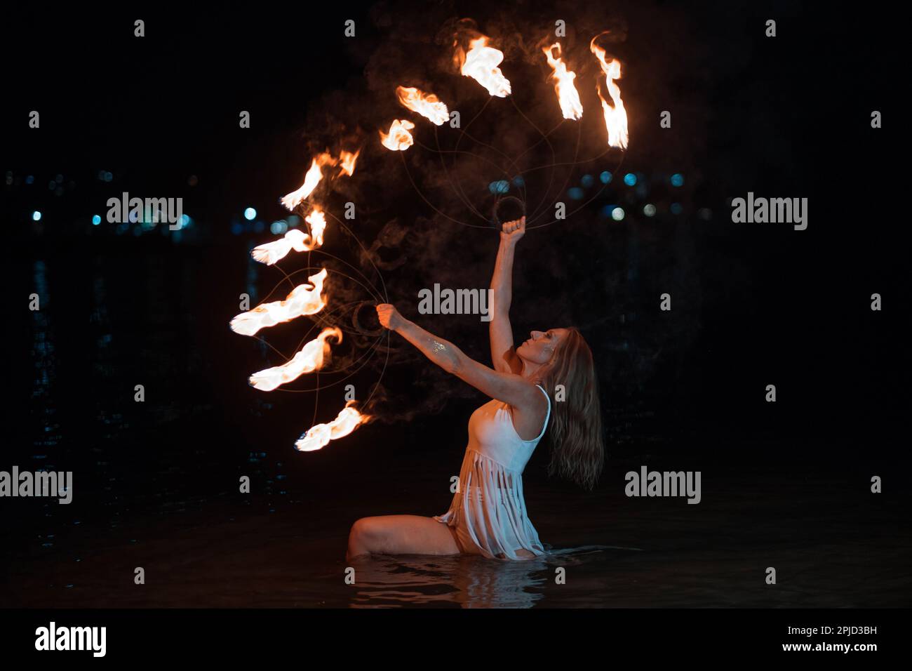 Caucasian woman dancing with fire in the water. Fire show at sea ...