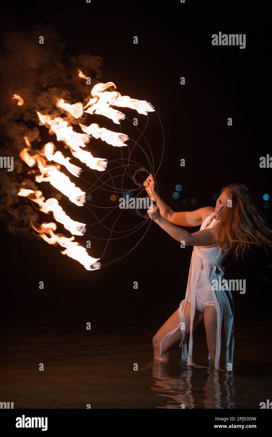 Caucasian woman dancing with fire in the water. Fire show at sea ...
