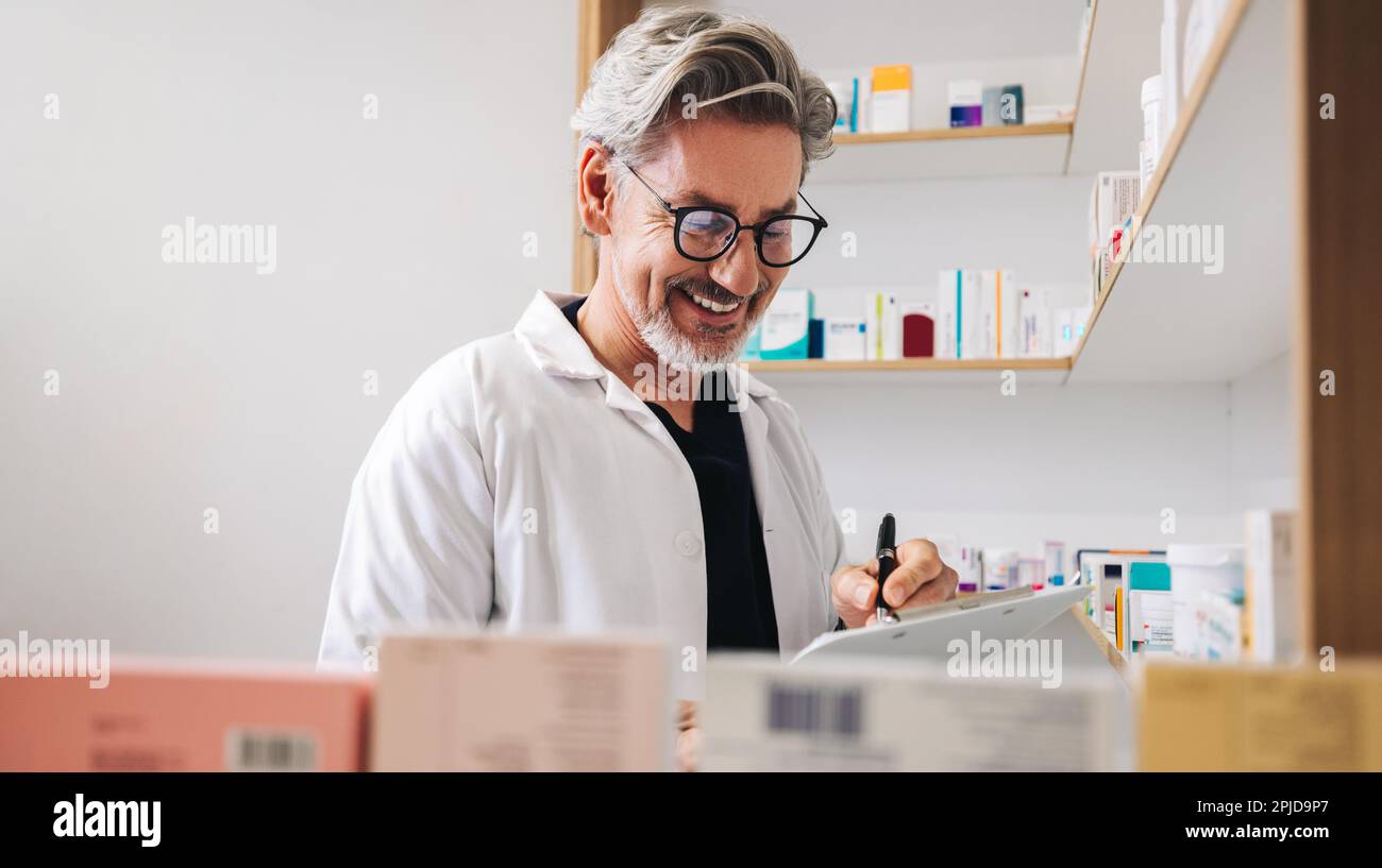 Male pharmacist writing on a clipboard while dispensing prescriptions ...
