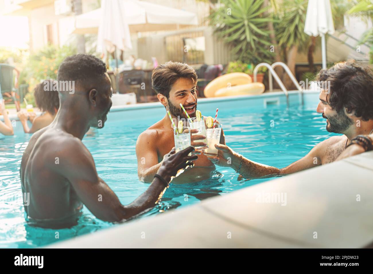 Three young men, one African and two Caucasian, chat and toast with ...
