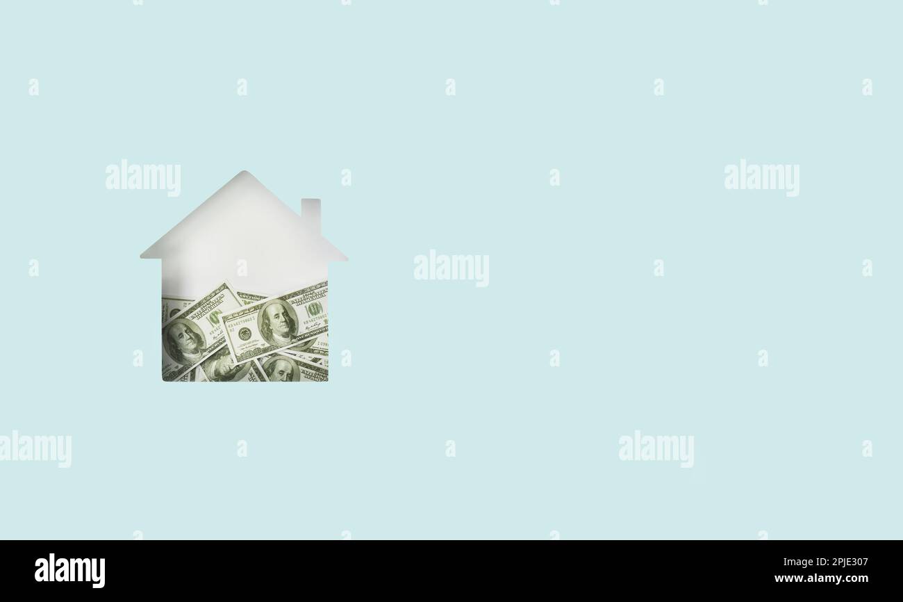 House shape cut out, half full with dollar bills, on blue background ...