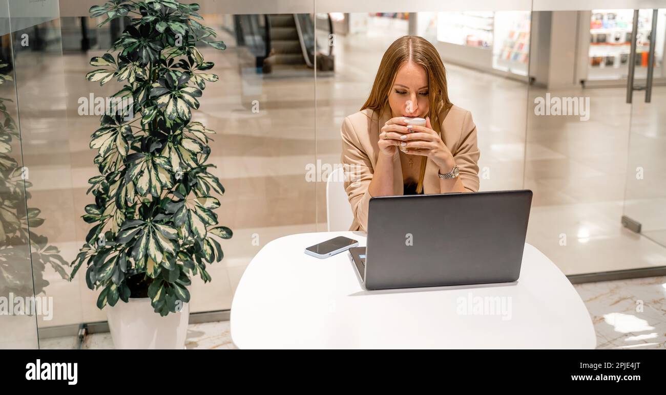 A business woman sits in a cafe, works at a computer, drinks coffee ...