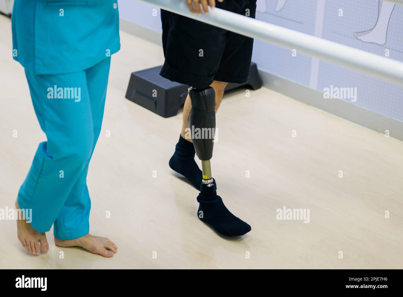 Physiotherapist helping patient with prosthetic leg at parallel bars ...