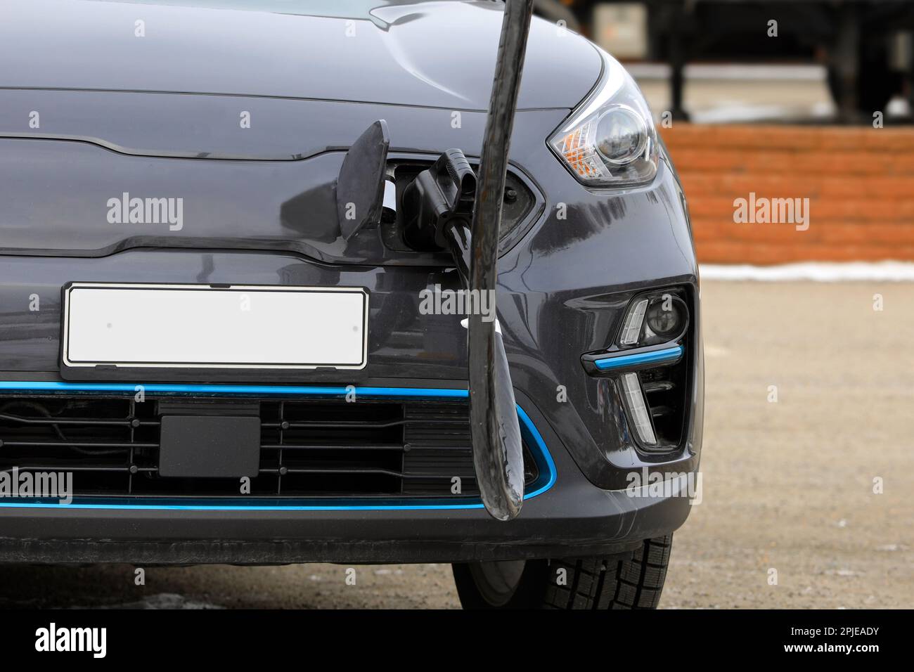 Electric car plugged in to recharge battery, detail, front view. No ...