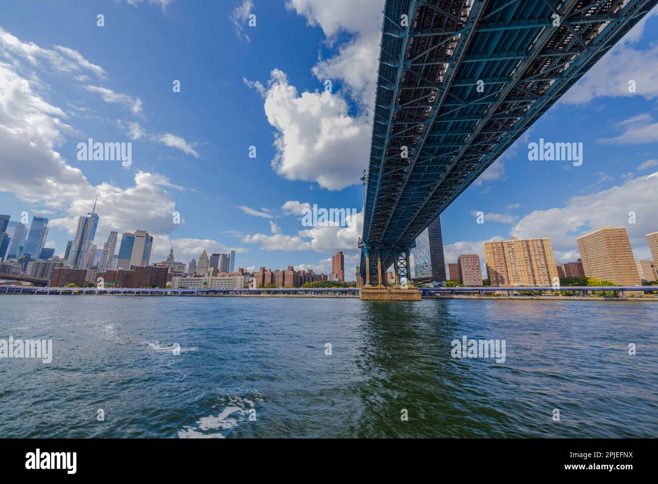 View of Brooklyn Bridge over Hudson River and skyscrapers of Manhattan against blue sky with ...