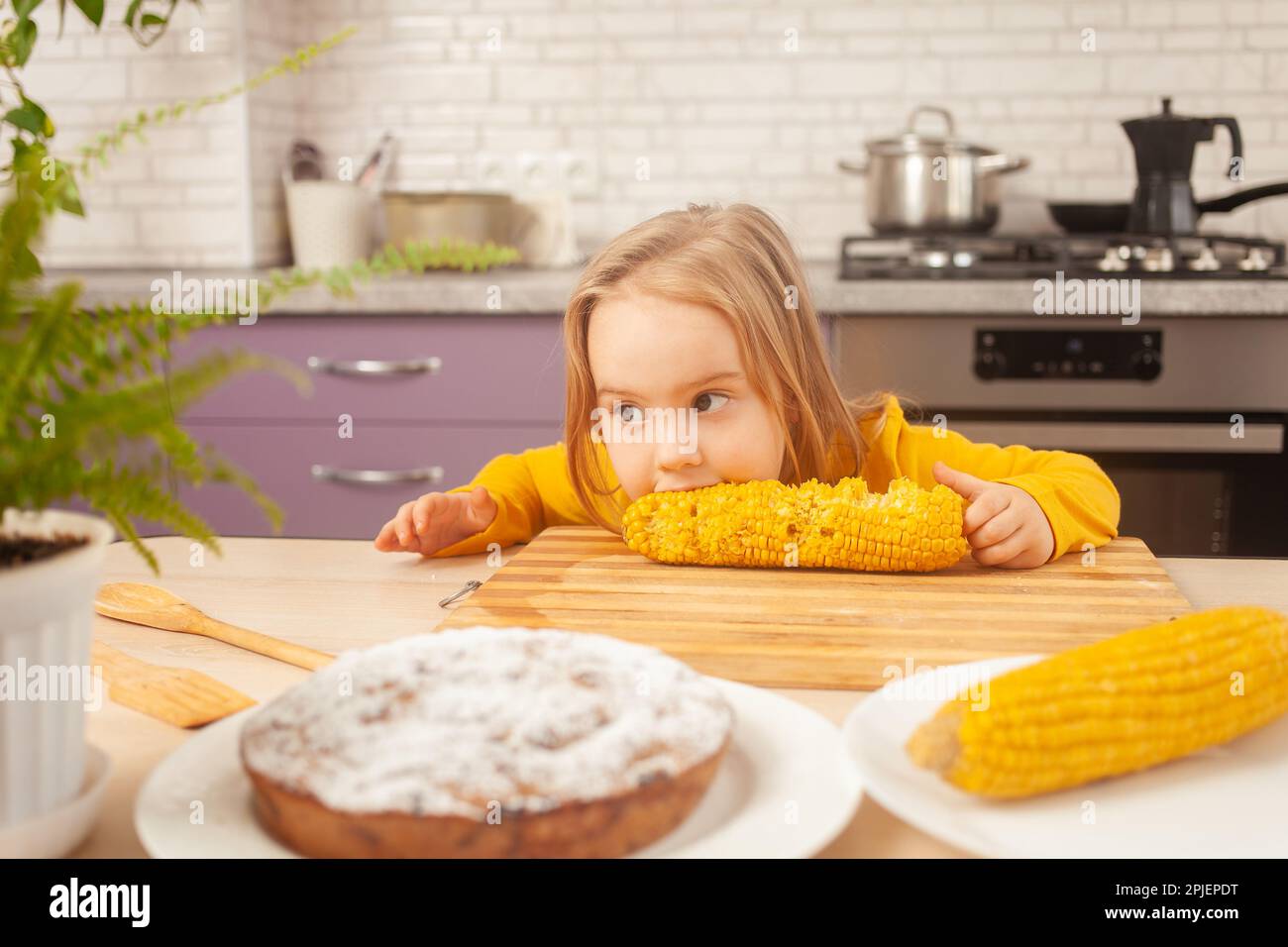 funny girl eats corn, indulges, lavender kitchen in background Stock ...