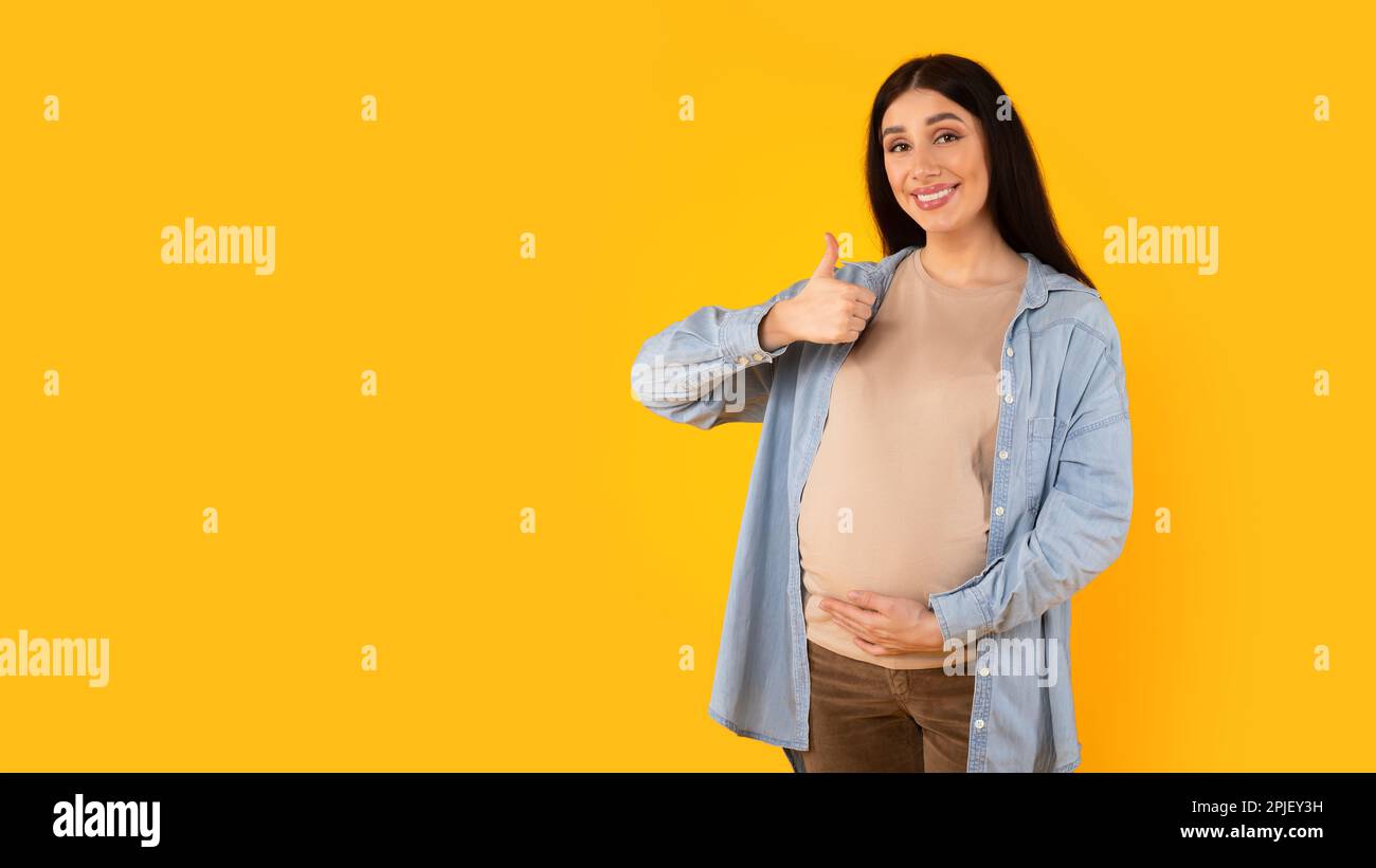 Excited pregnant woman touching belly, showing thumb up and approving ...