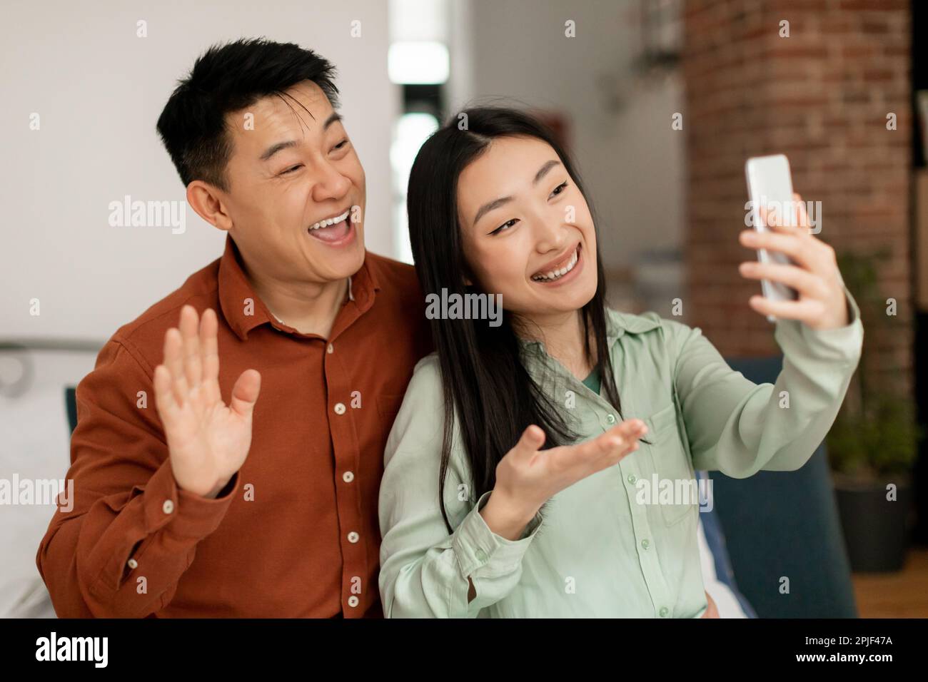 Excited korean couple using mobile phone, video calling in living room ...