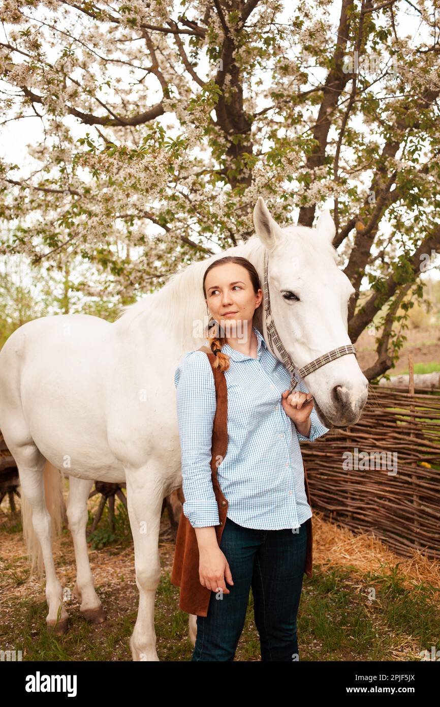 A beautiful young woman poses next to a white horse. Cowboy, ranch ...