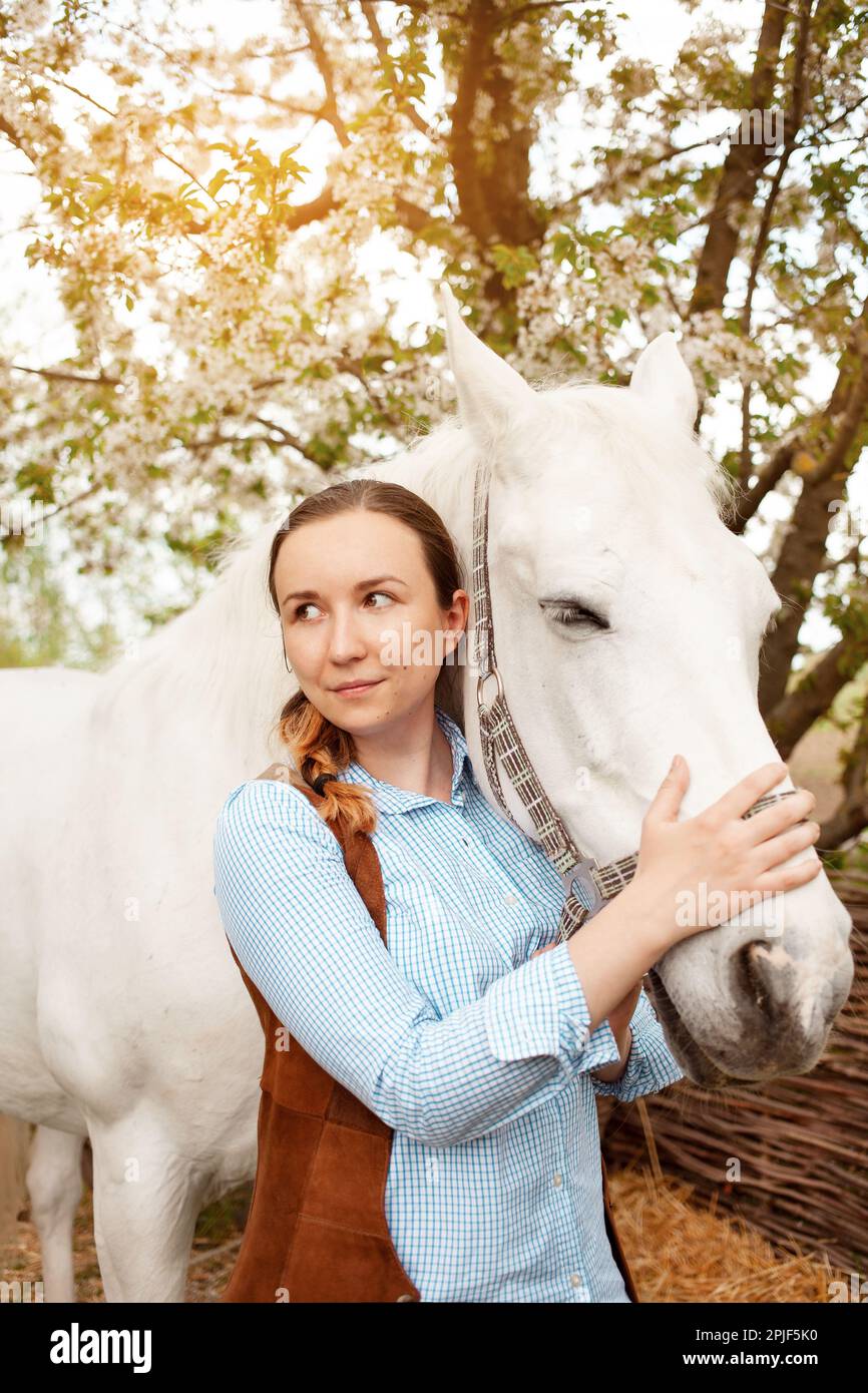 A beautiful young woman poses next to a white horse. Cowboy, ranch ...