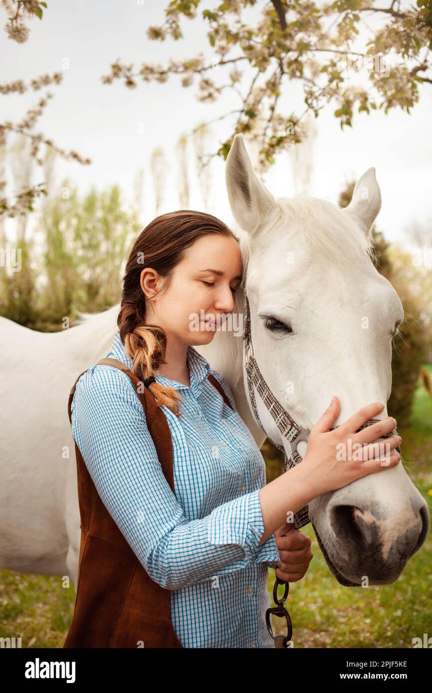 A beautiful young woman poses next to a white horse. Cowboy, ranch ...