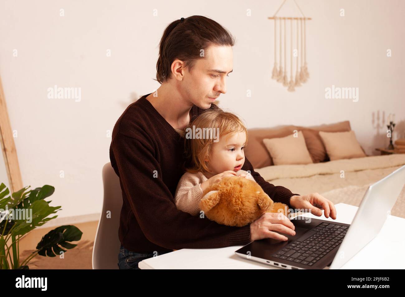A man works at home on a laptop. The child distracts from work, misses ...
