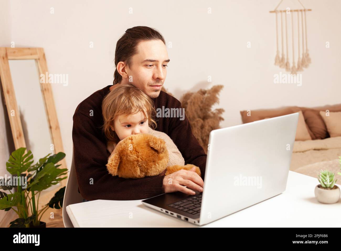 A man works at home on a laptop. The child distracts from work, misses ...