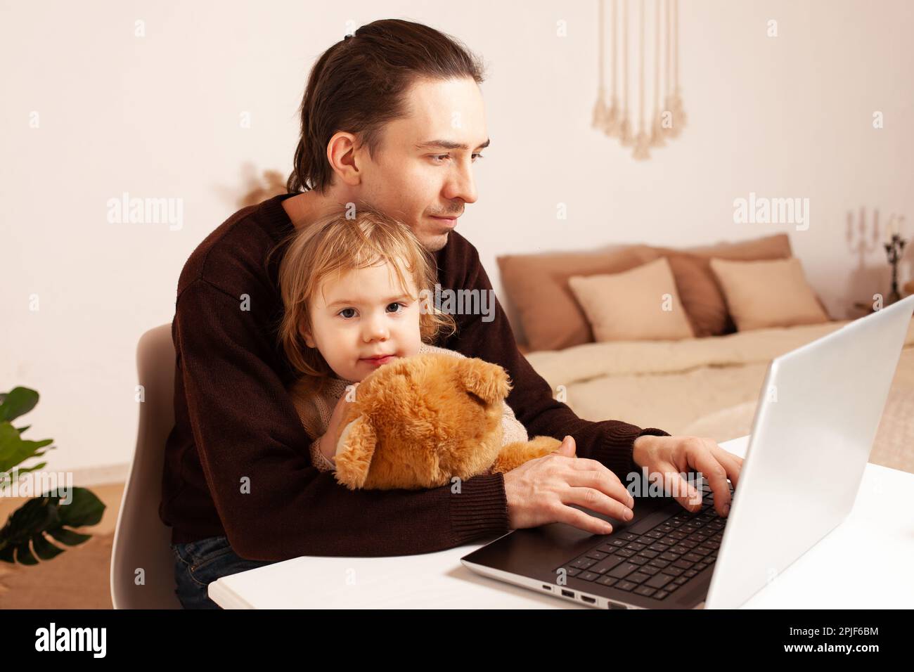 A man works at home on a laptop. The child distracts from work, misses ...