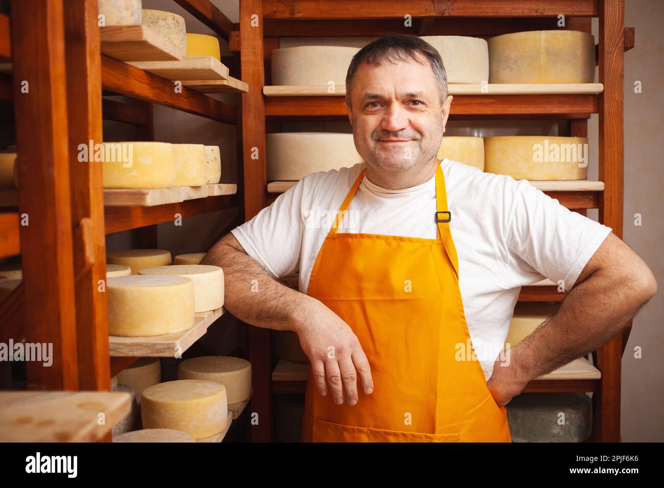 A man cheesemaker in the cellar, beautiful wooden shelves with a ready ...
