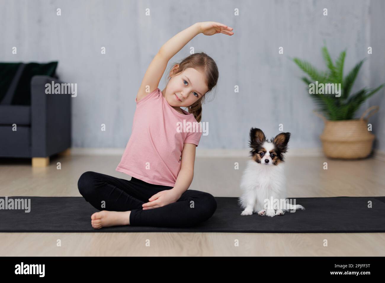 cute little girl doing stretching exercises, sitting with her puppy ...