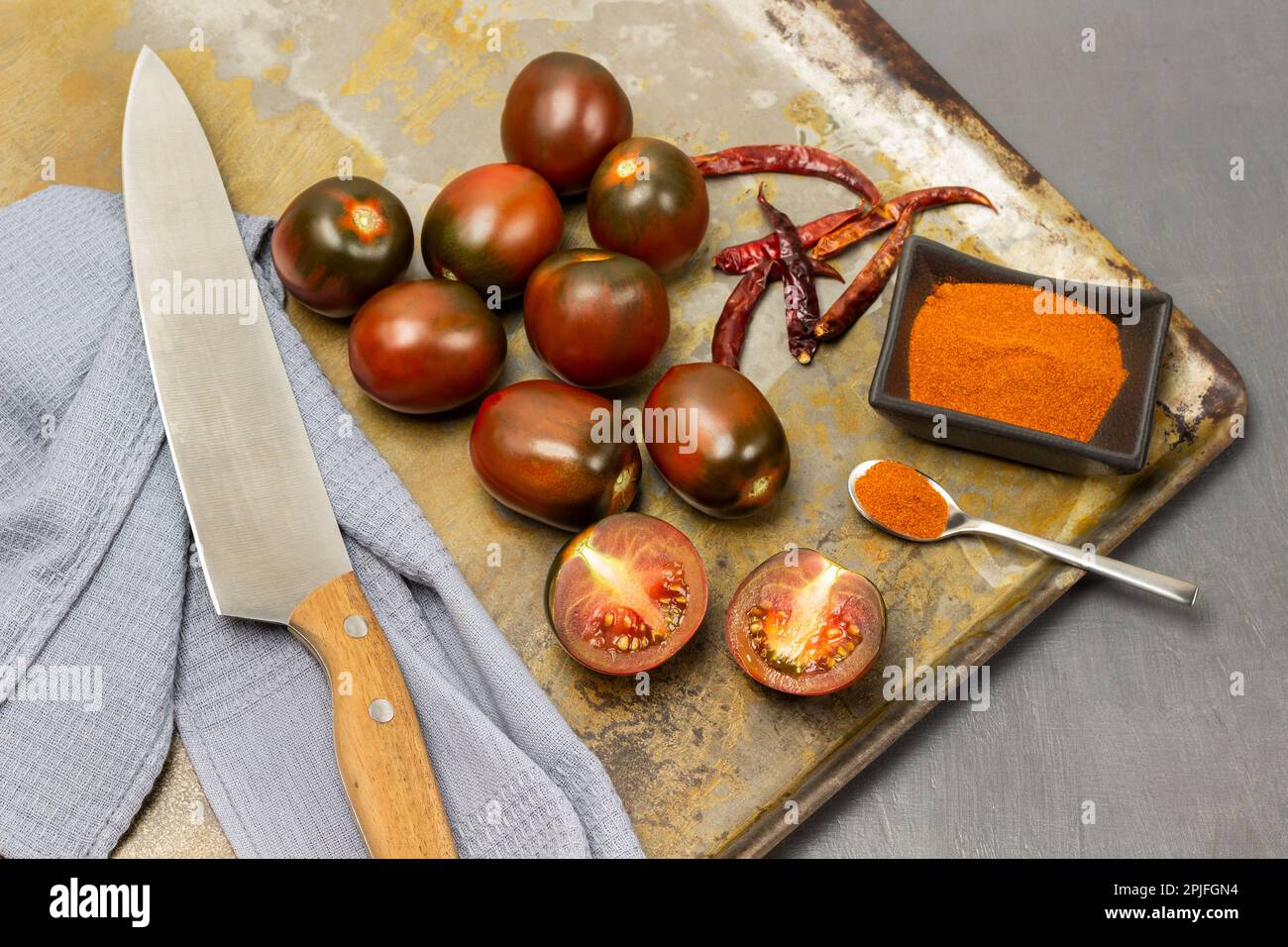 Red tomatoes, ground pepper in a bowl and pepper pods on a rusty tray ...