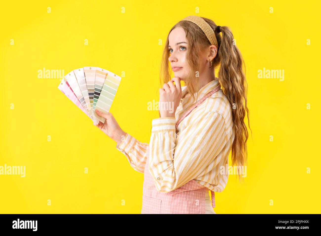 Thoughtful female artist with paint color palettes on yellow background ...