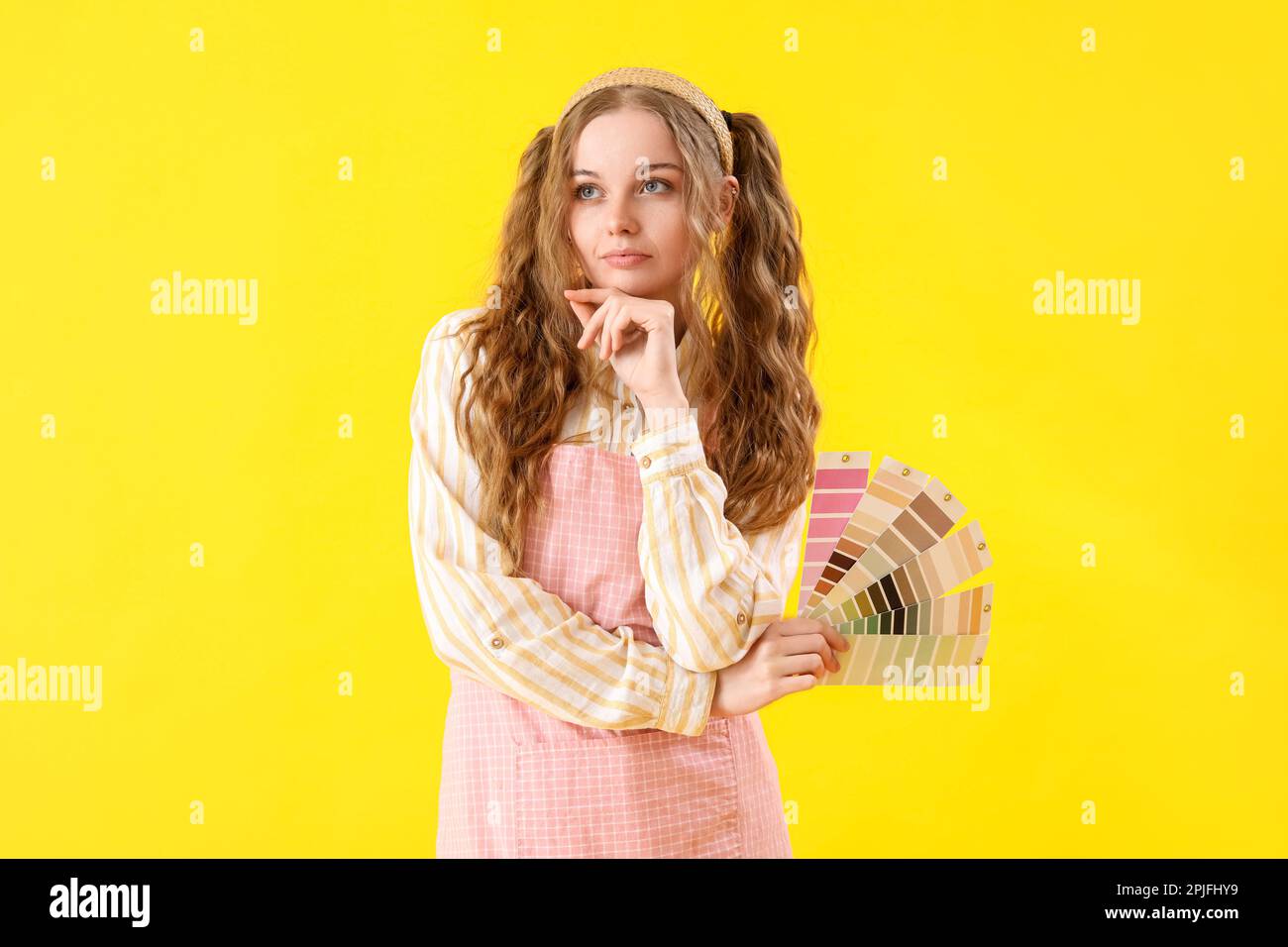 Thoughtful female artist with paint color palettes on yellow background ...