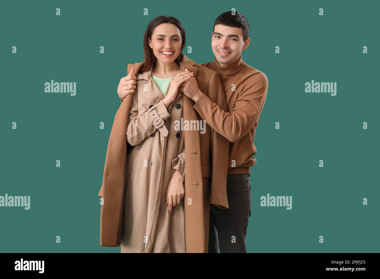 Young man putting coat onto his girlfriend on green background Stock ...