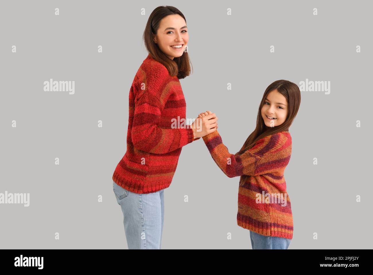 Little girl and her mother in warm sweaters holding hands on grey ...