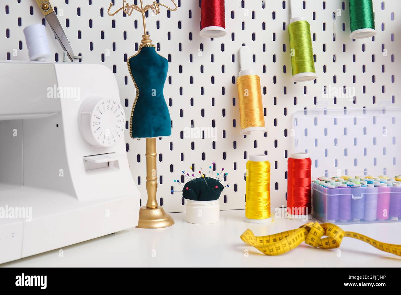 Sewing machine, mannequin and pegboard with thread spools on table in ...
