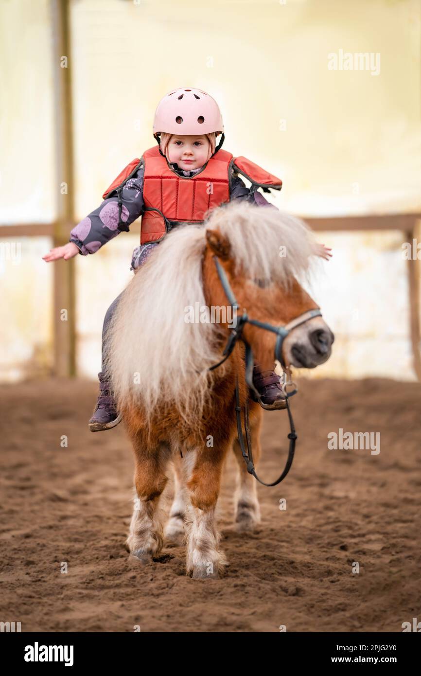 Little Child Riding Lesson. Three-year-old girl rides a pony and does ...
