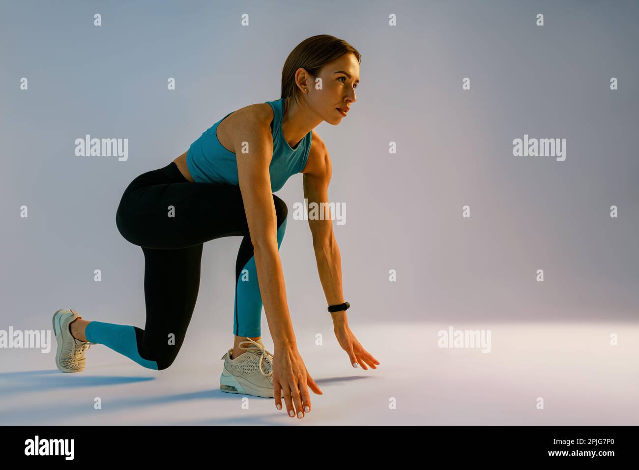 Sporty woman in starting position ready for running looking at side on ...