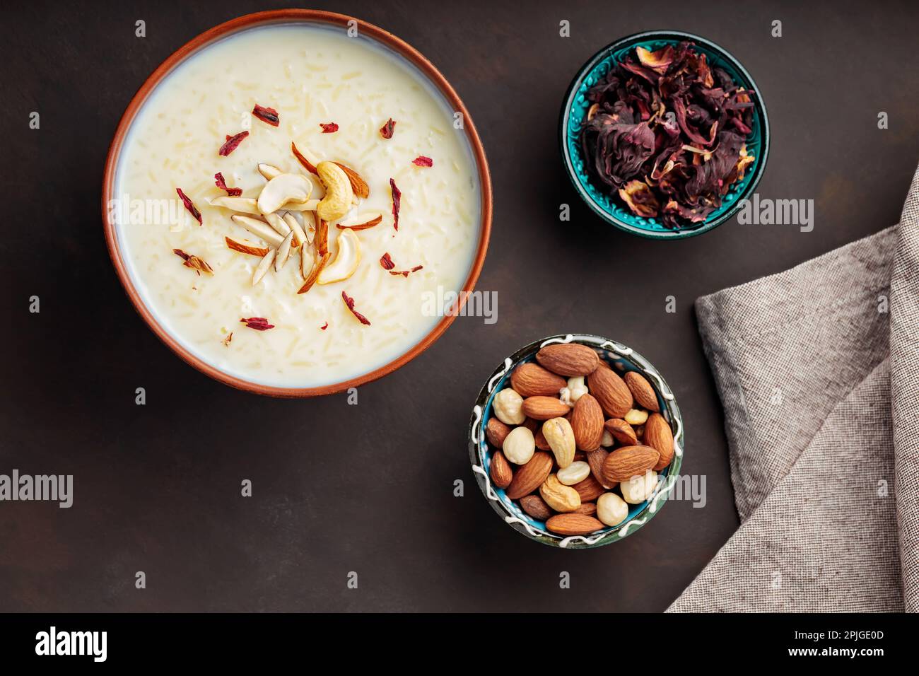 Rice kheer, nuts and dried hibiscus flowers on a dark background ...