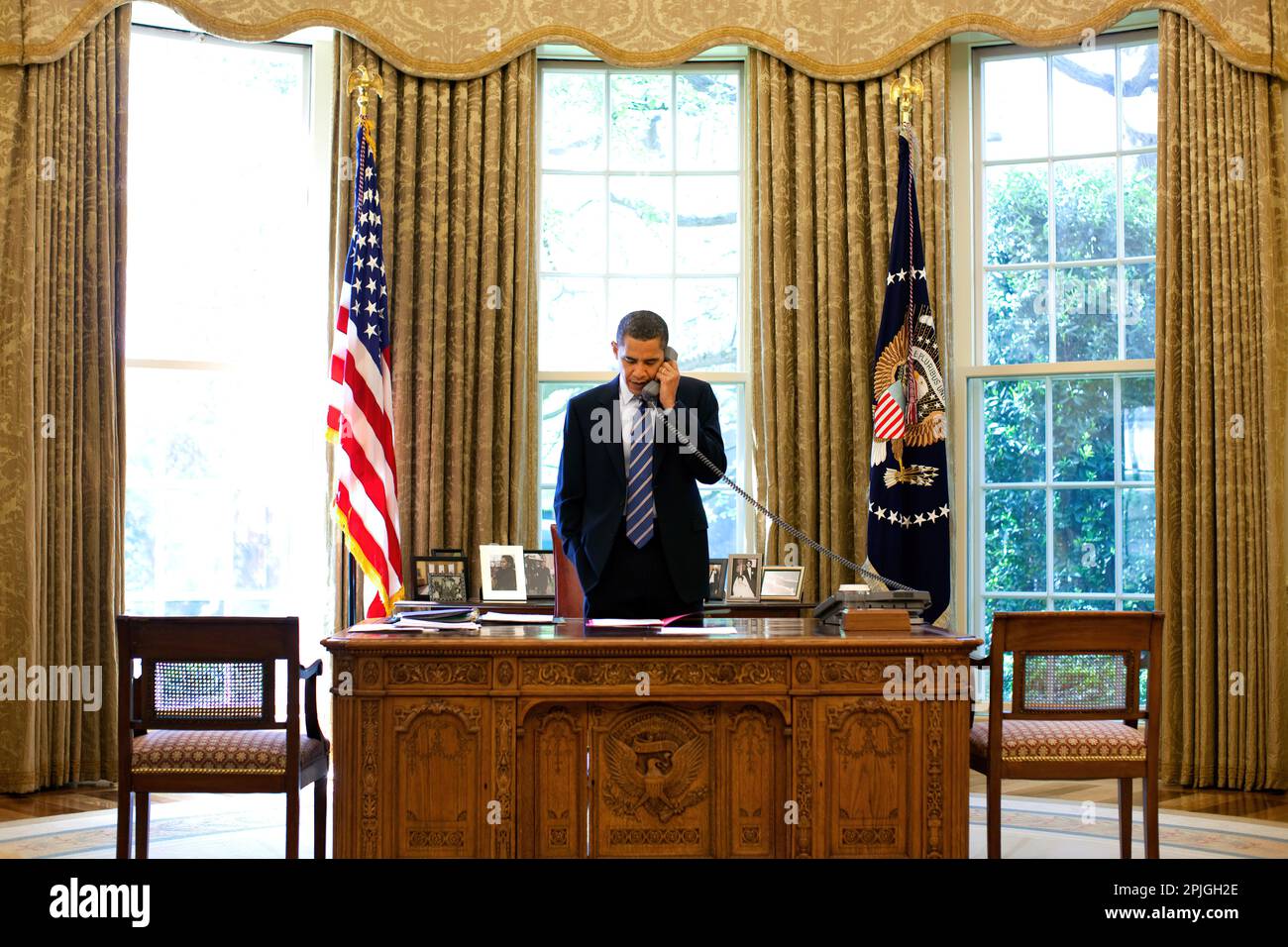 President Barack Obama stands at his desk while talking on the phone ...