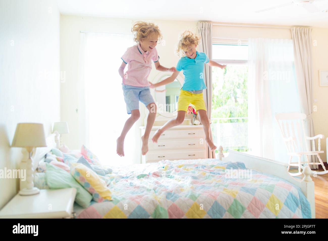 Child jumping on bed in white bedroom with big window. Kids play at ...