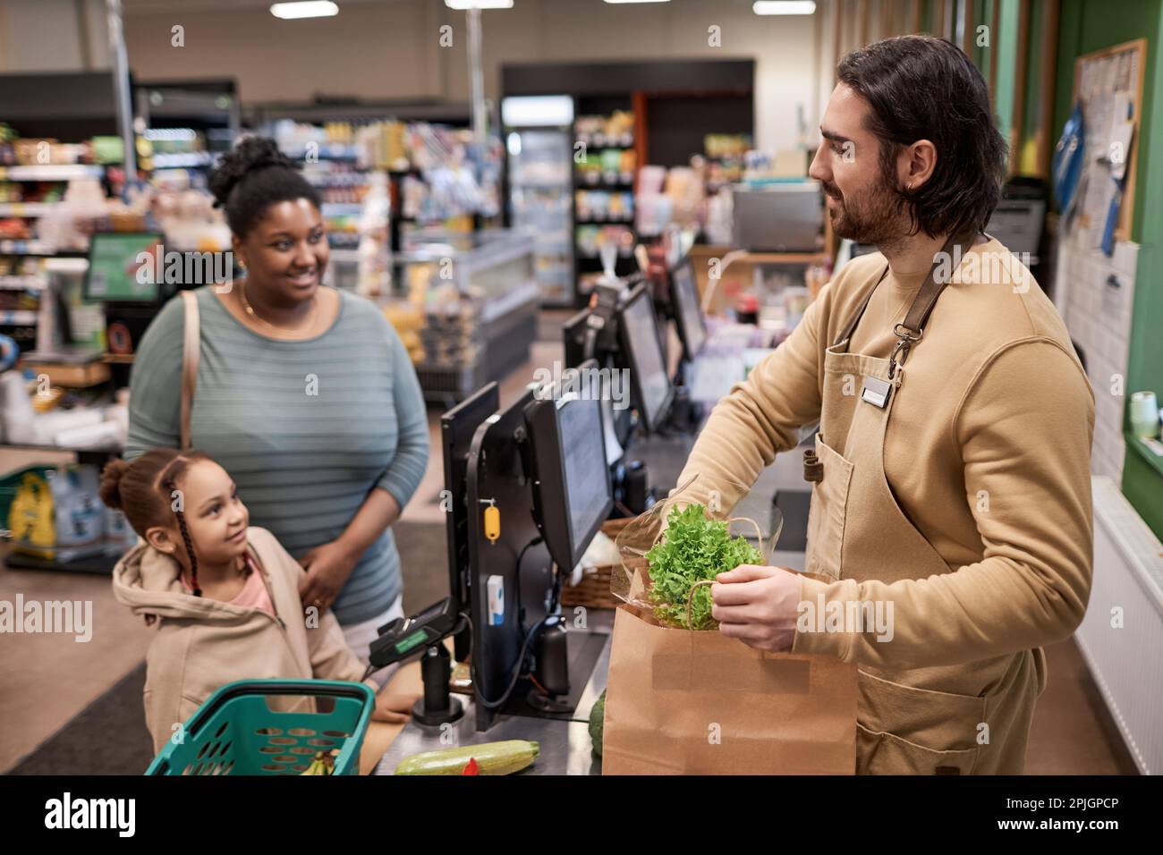 Side view portrait of smiling male worker in supermarket helping young ...