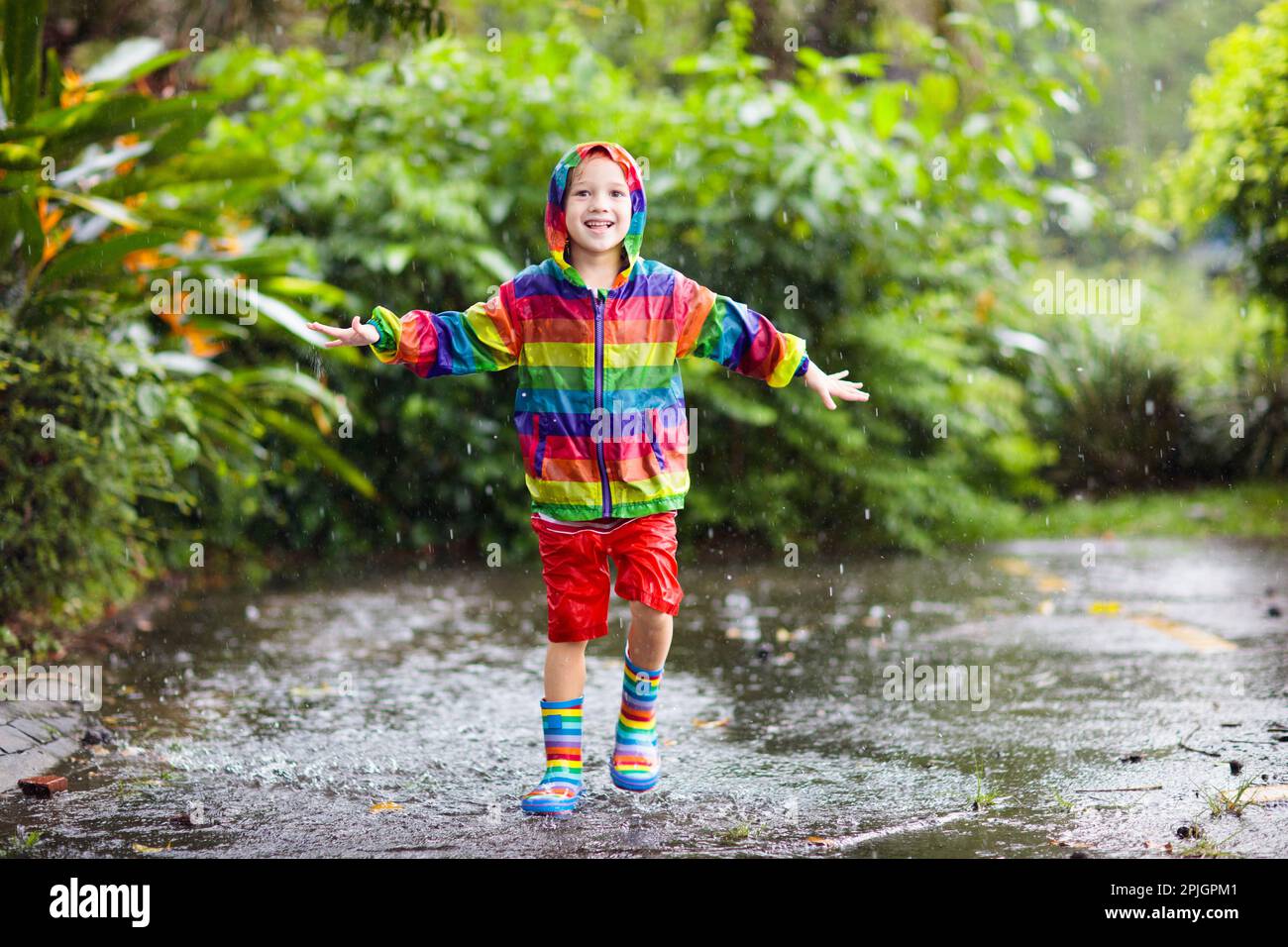 Kid playing in the rain in autumn park. Child jumping in muddy puddle ...