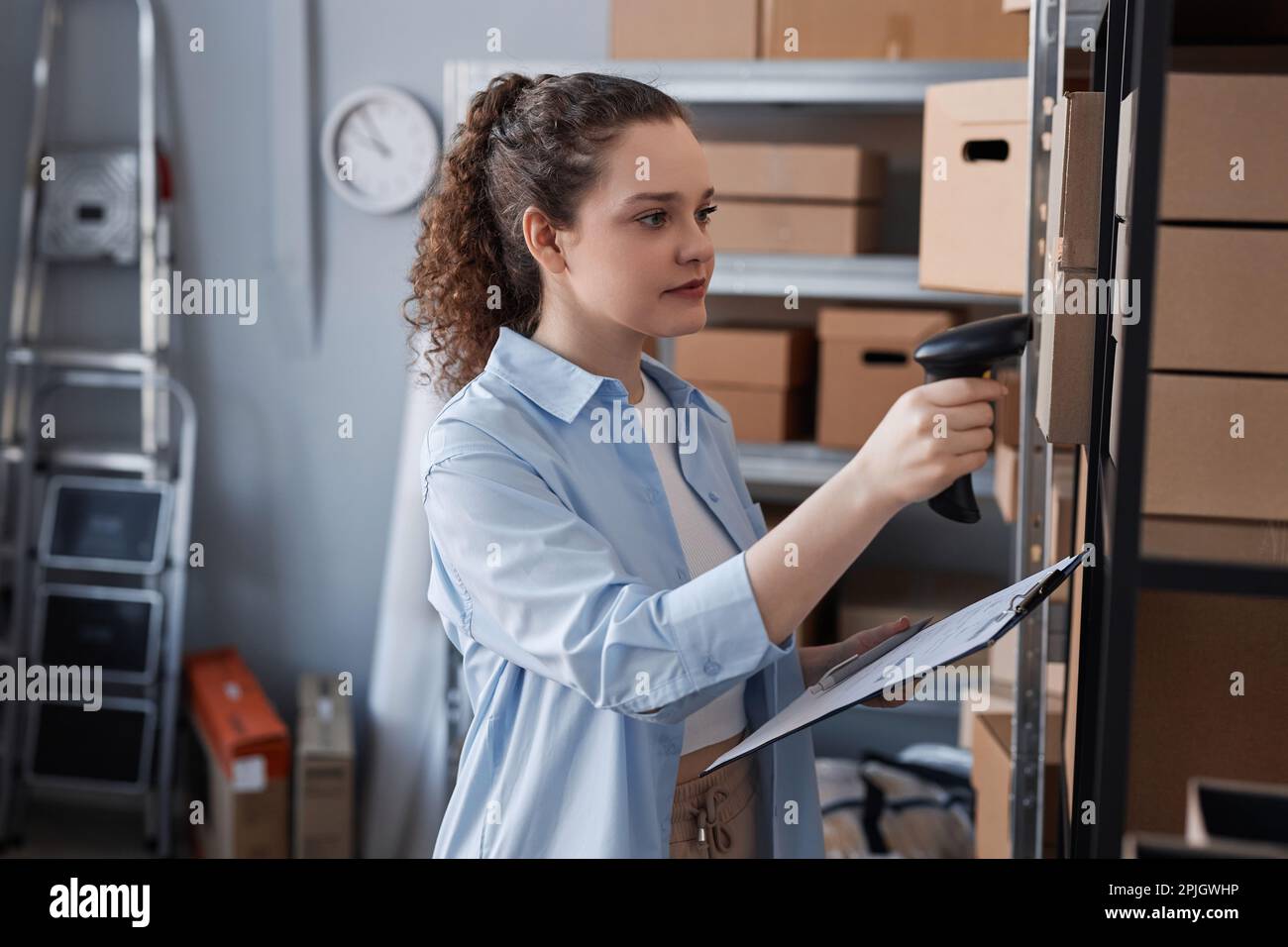 Young woman in casualwear scanning qr codes on packed cardboard boxes with orders standing on ...