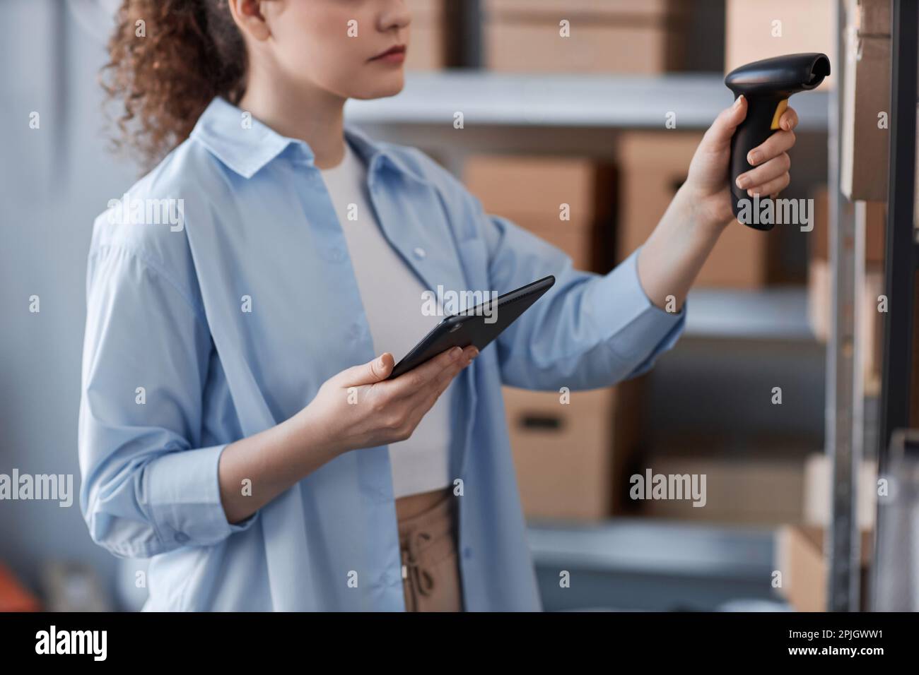 Close-up of young woman in blue shirt scanning qr codes on packed boxes ...