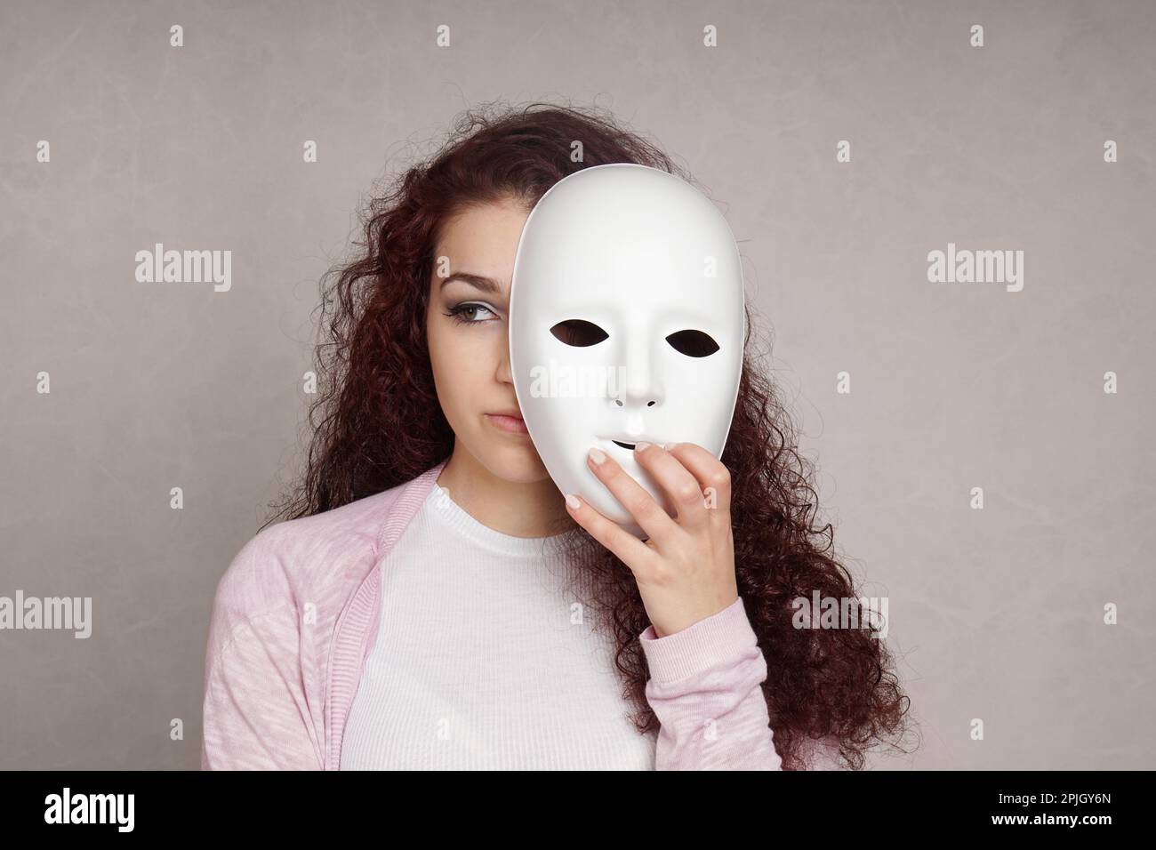 sad young woman hiding her face behind mask, identity or personality ...
