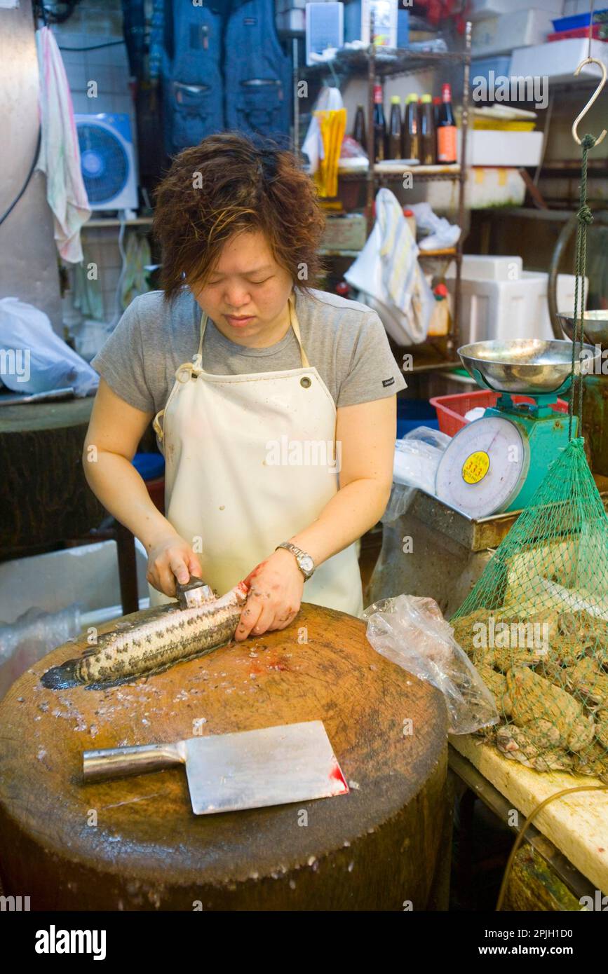 Woman preparing fish next to frogs in a net at the fish market, Kowloon ...
