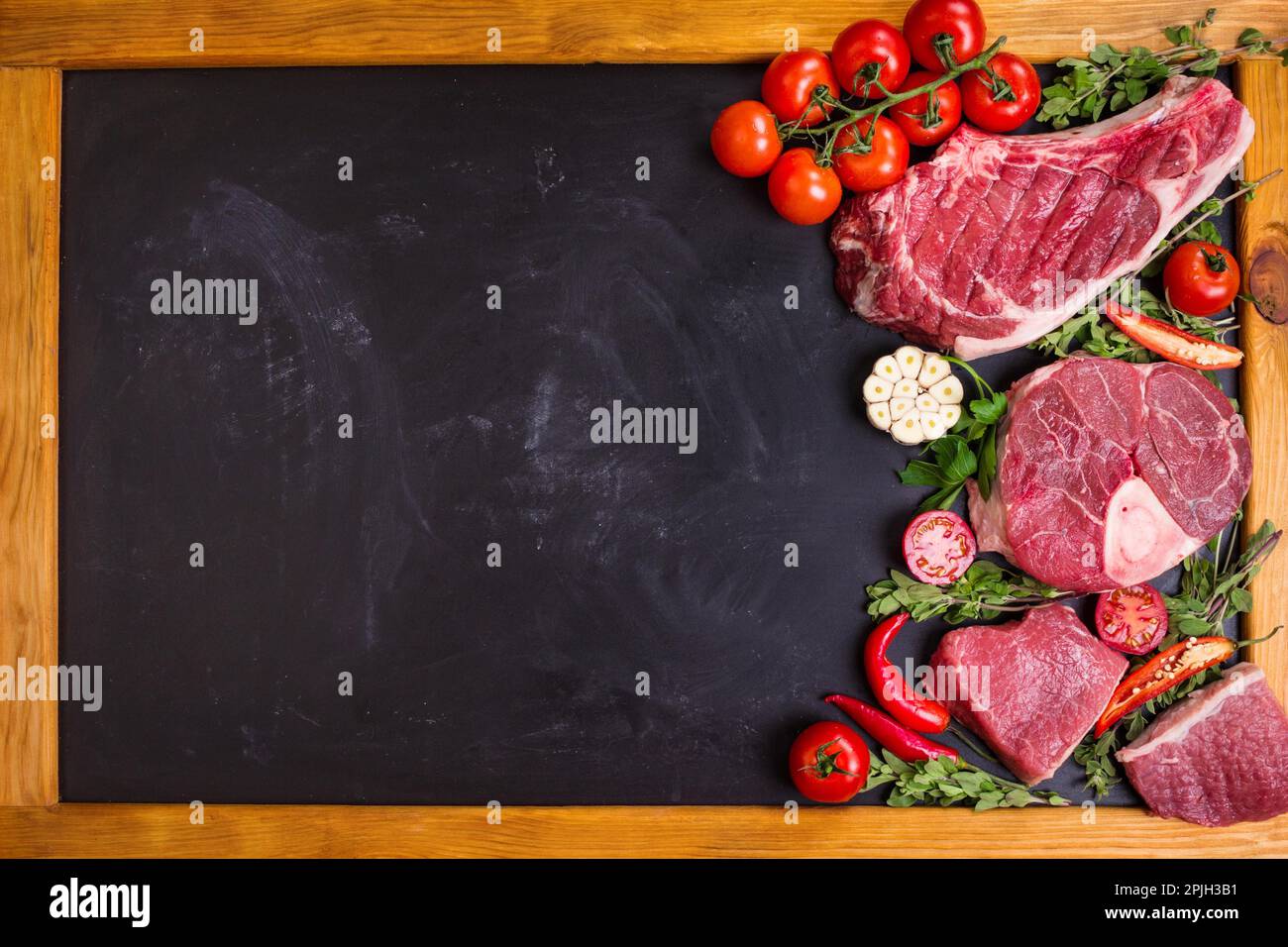 Raw juicy meat steaks on a black chalk board background with wooden ...