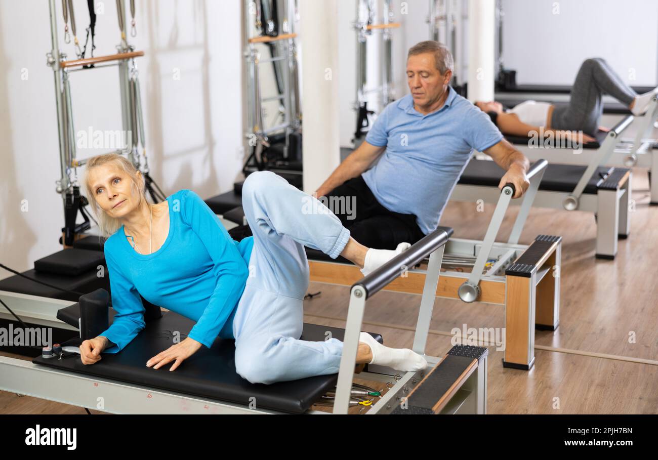 Elderly woman doing toning exercise for back on Pilates reformer bed in ...