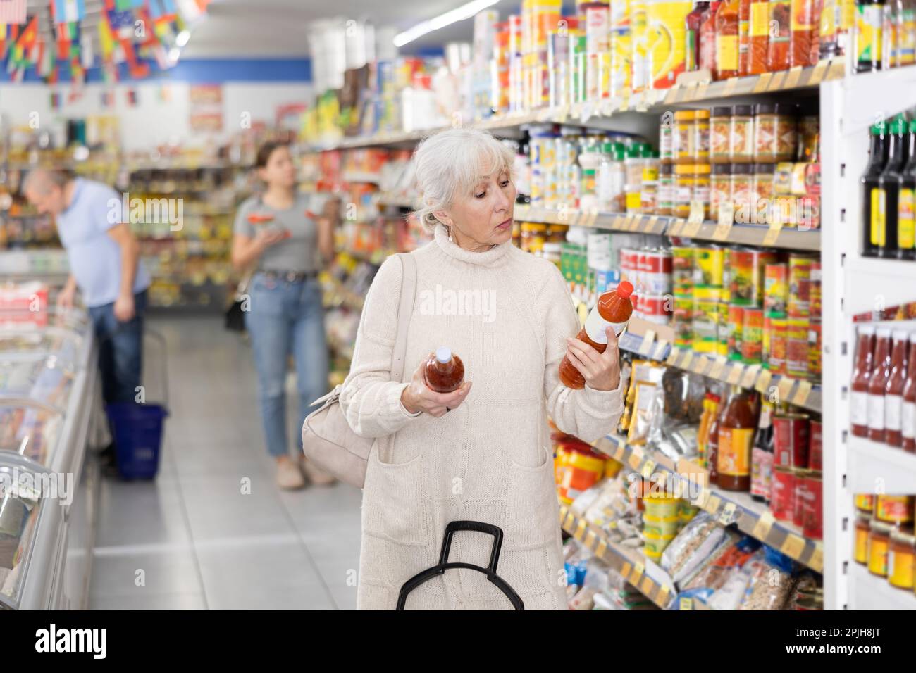 Elderly woman reading labels on bottles with sauce in supermarket Stock ...