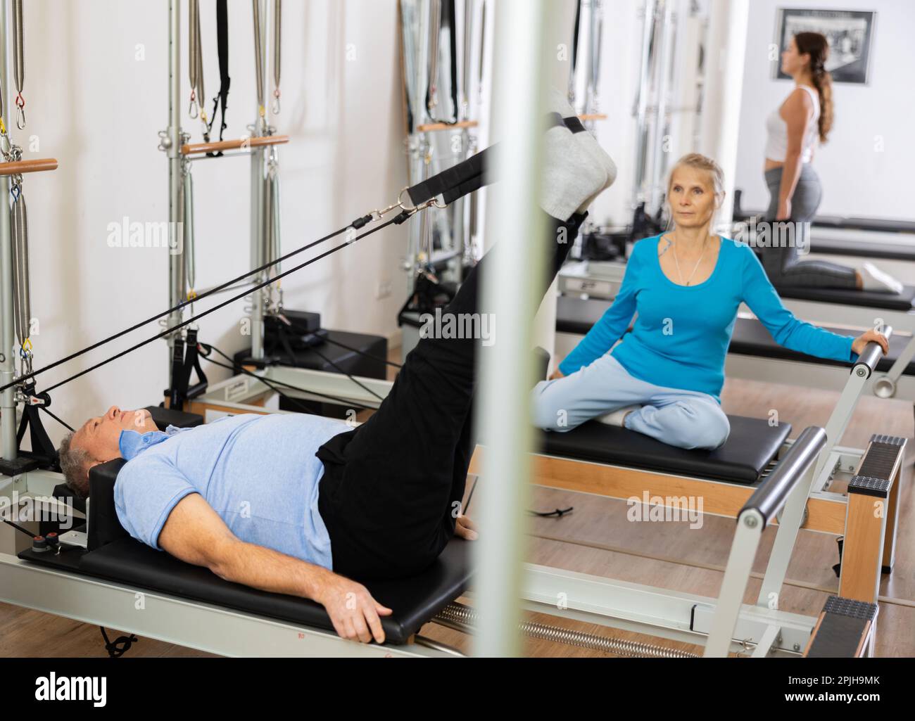Focused old man performing stretching Pilates exercises with reformer ...