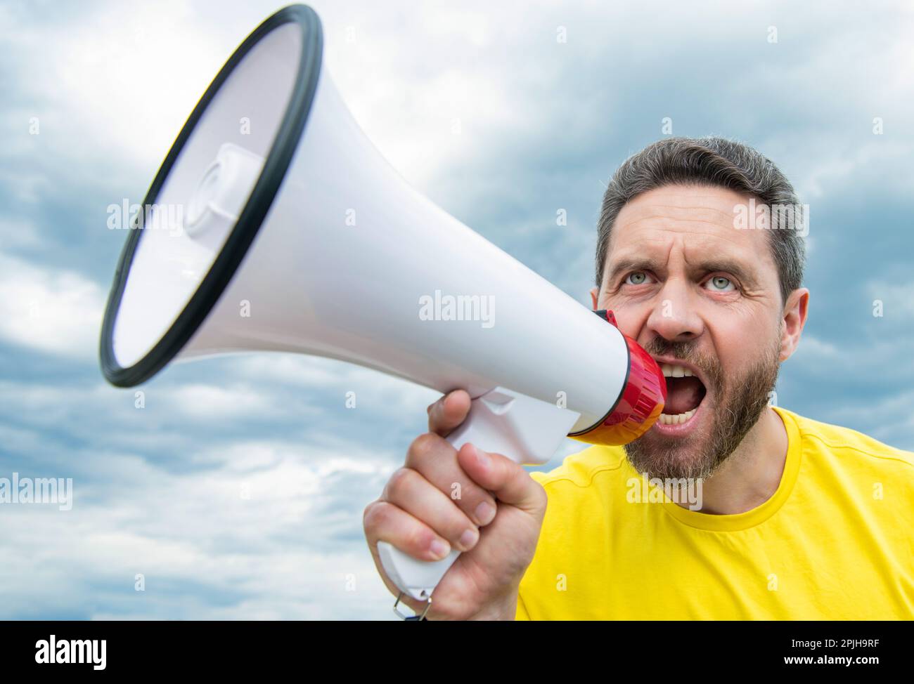 man in yellow shirt shout in loudspeaker on sky background. voice ...
