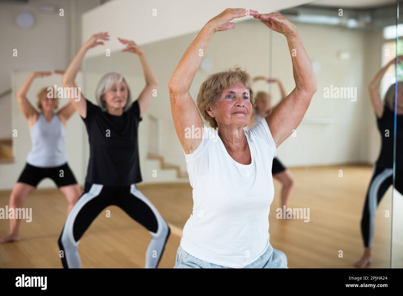 Mature women perform a plie squat while in the position of a ballet ...